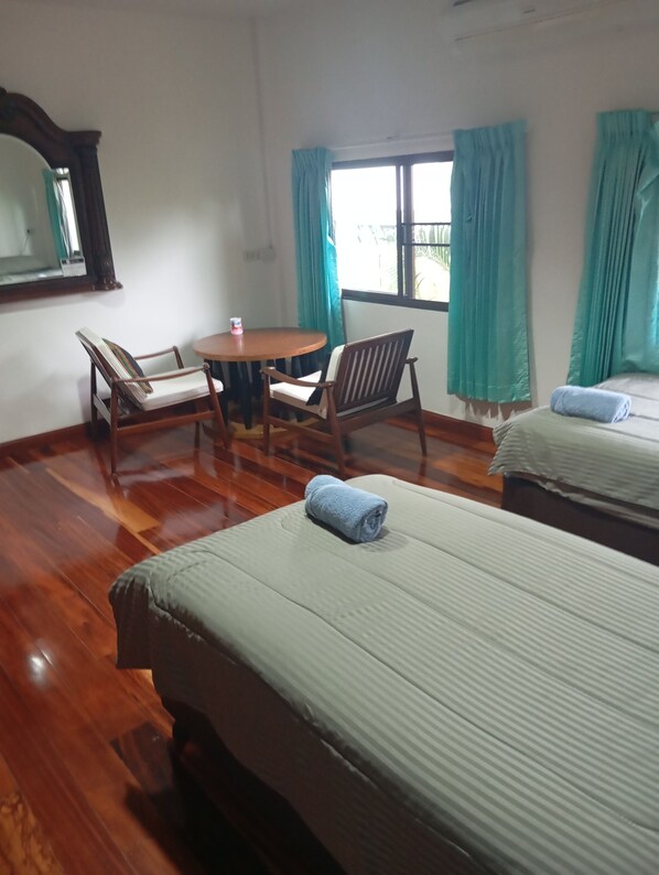 Quarto de hotel com duas camas, piso de madeira, mesa redonda com cadeiras e janela com cortinas.