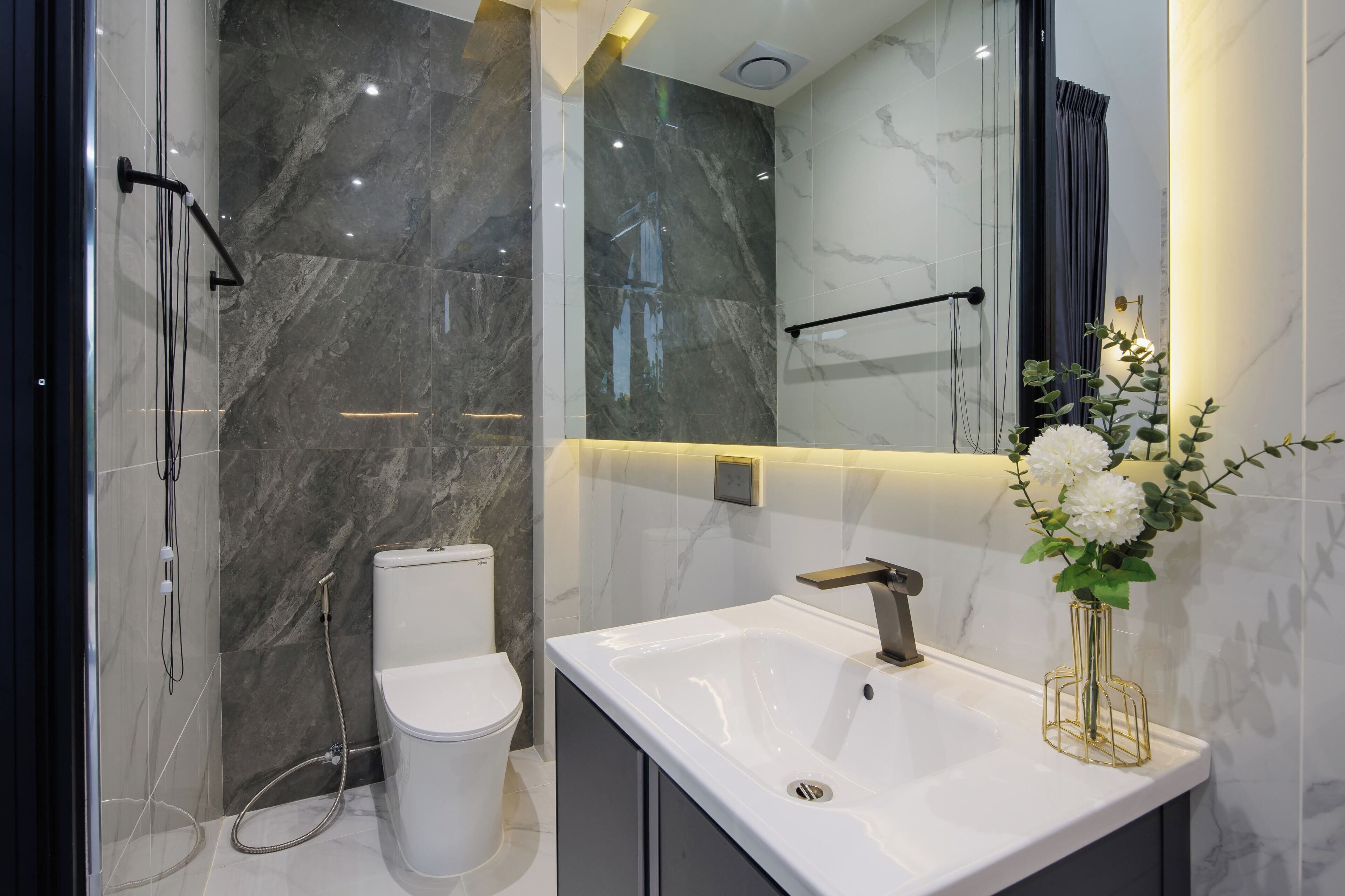 Casa de banho moderna com chuveiro de mármore, sanita branca e lavatório com um vaso dourado.