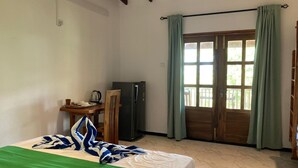 Quarto com cama, escrivaninha, frigorífico e janela com cortinas.