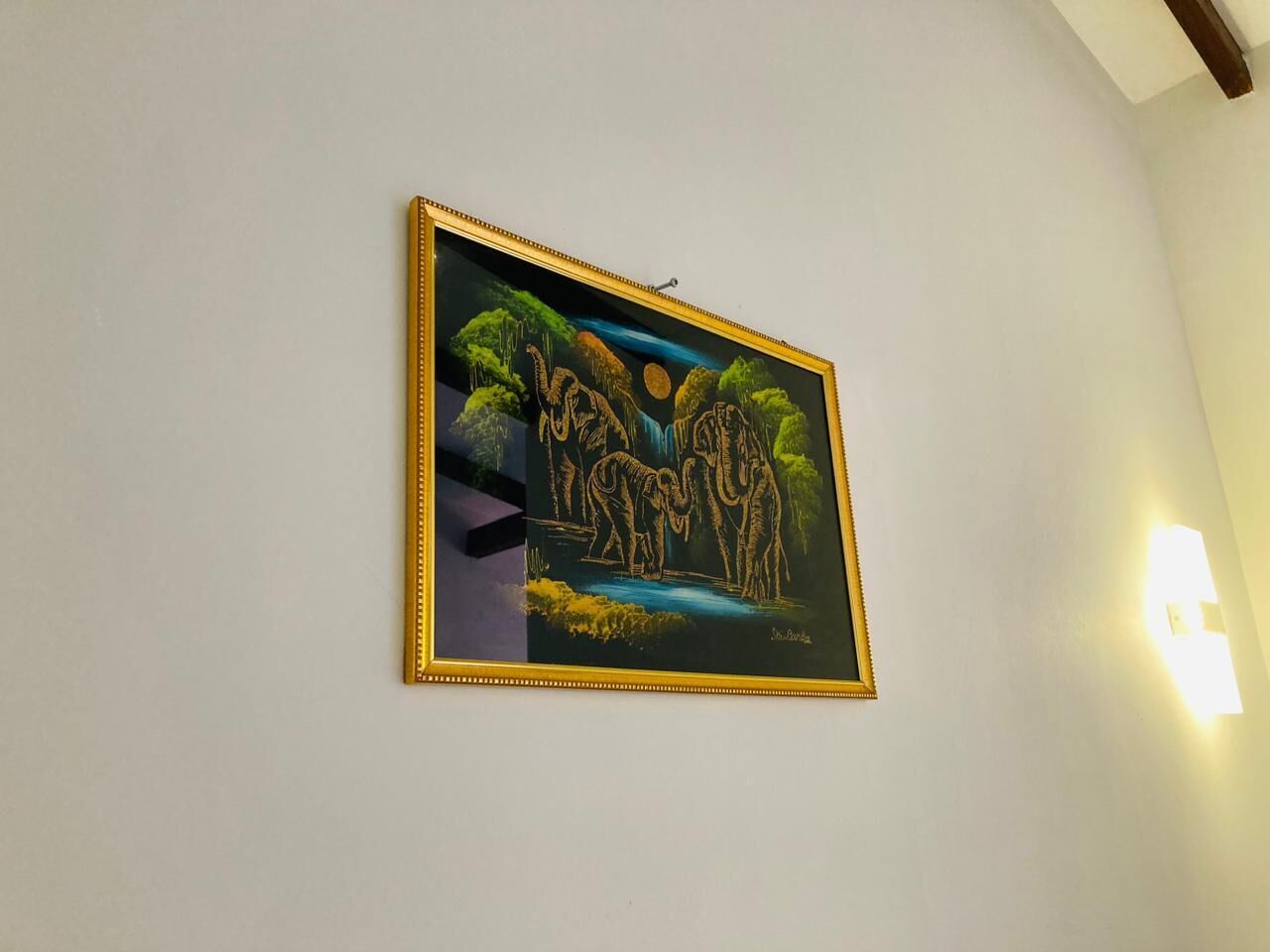 Obra emoldurada mostrando elefantes e árvores numa parede.