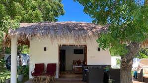 Área externa com cobertura de palha, mobiliário de vime e vista para o interior da casa.