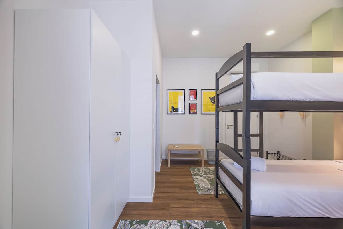 Quarto com beliche, piso de madeira, um banco e quadros nas paredes.