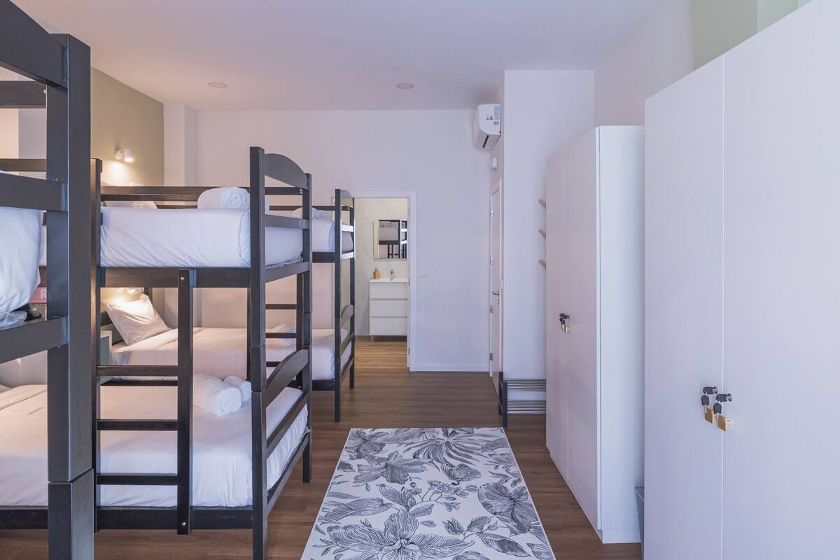 Quarto com beliche, piso de madeira, tapete estampado e guarda-roupa branco.