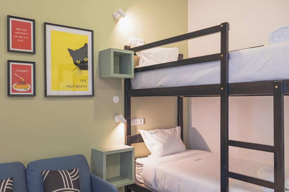 Quarto com beliche, uma pequena escrivaninha, sofá e pôsteres emoldurados na parede.
