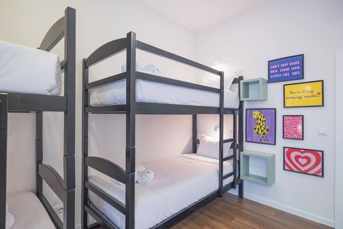 Quarto com beliches, roupa de cama branca e parede com pôsteres motivacionais.