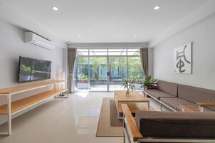 Uma sala de estar moderna com televisão de tela plana, móveis de madeira, um sofá e uma janela grande com vista para o verde.