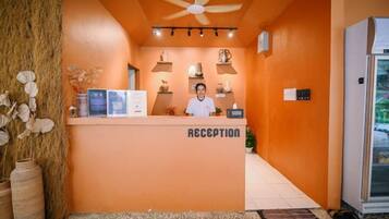 Área de recepção com recepcionista, ventilador de teto e placa com a inscrição 'RECEPTION'.