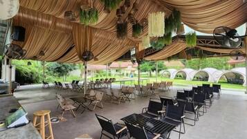 Uma área externa com mesas, cadeiras, um bar e vista para o verde.