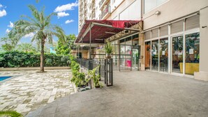 Um hotel com área externa coberta, piscina e plantas em vasos.