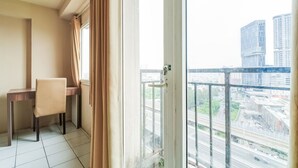 Quarto com escrivaninha, cadeira e vista para a paisagem urbana através de uma grande janela.