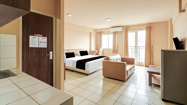 Quarto de hotel com cama, sofá, mesa, geladeira e banheiro com chuveiro.