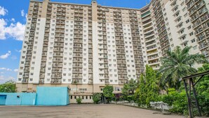 Um edifício residencial alto com várias varandas, um portão azul e vegetação ao redor.