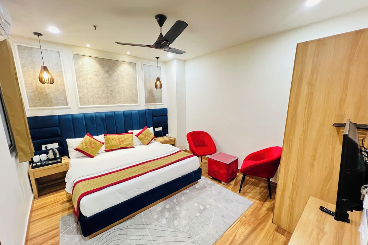 Quarto de hotel moderno com uma cama grande, duas cadeiras vermelhas, uma escrivaninha de madeira e um ventilador de teto.
