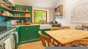 Cozinha com armários verdes, uma mesa de madeira e janela com vista para vegetação.