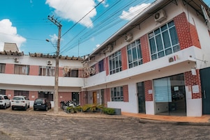 Um edifício com vários andares, área de estacionamento, espaço coberto para sentar ao ar livre e fachada com porta de vidro.