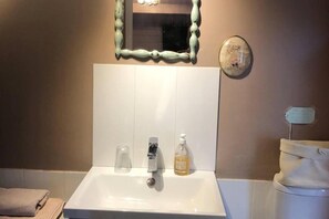 Casa de banho com lavatório branco, espelho, dispensador de sabão e porta-toalhas.