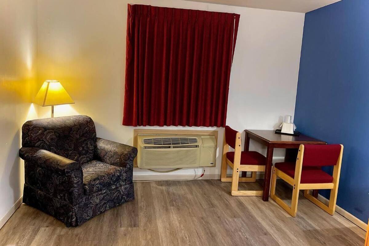 Um quarto pequeno com sofá, mesa e cadeiras, cortina vermelha e aquecedor fixado na parede.