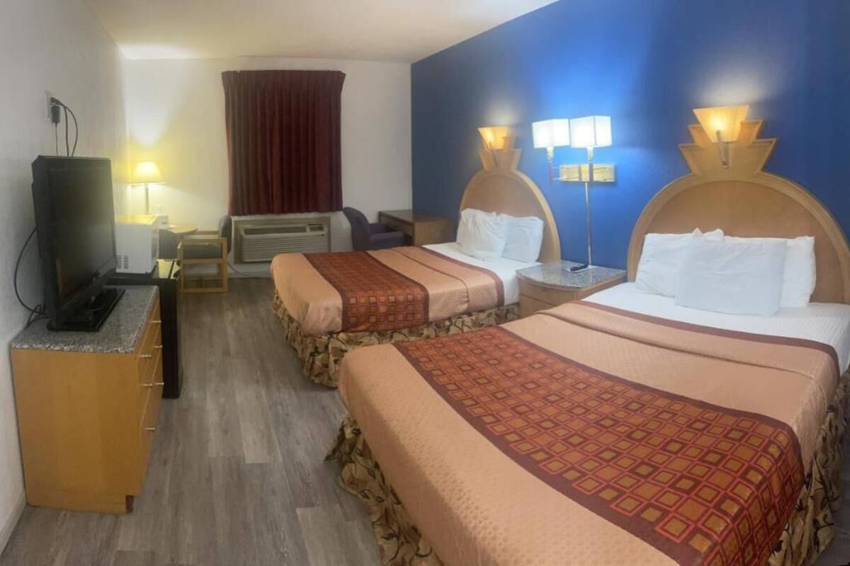Quarto de hotel com duas camas, televisão, escrivaninha e uma cadeira.