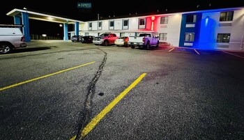 Um motel com uma fileira de carros estacionados, uma rachadura visível no estacionamento e um prédio com uma placa que diz "EXPRESS".