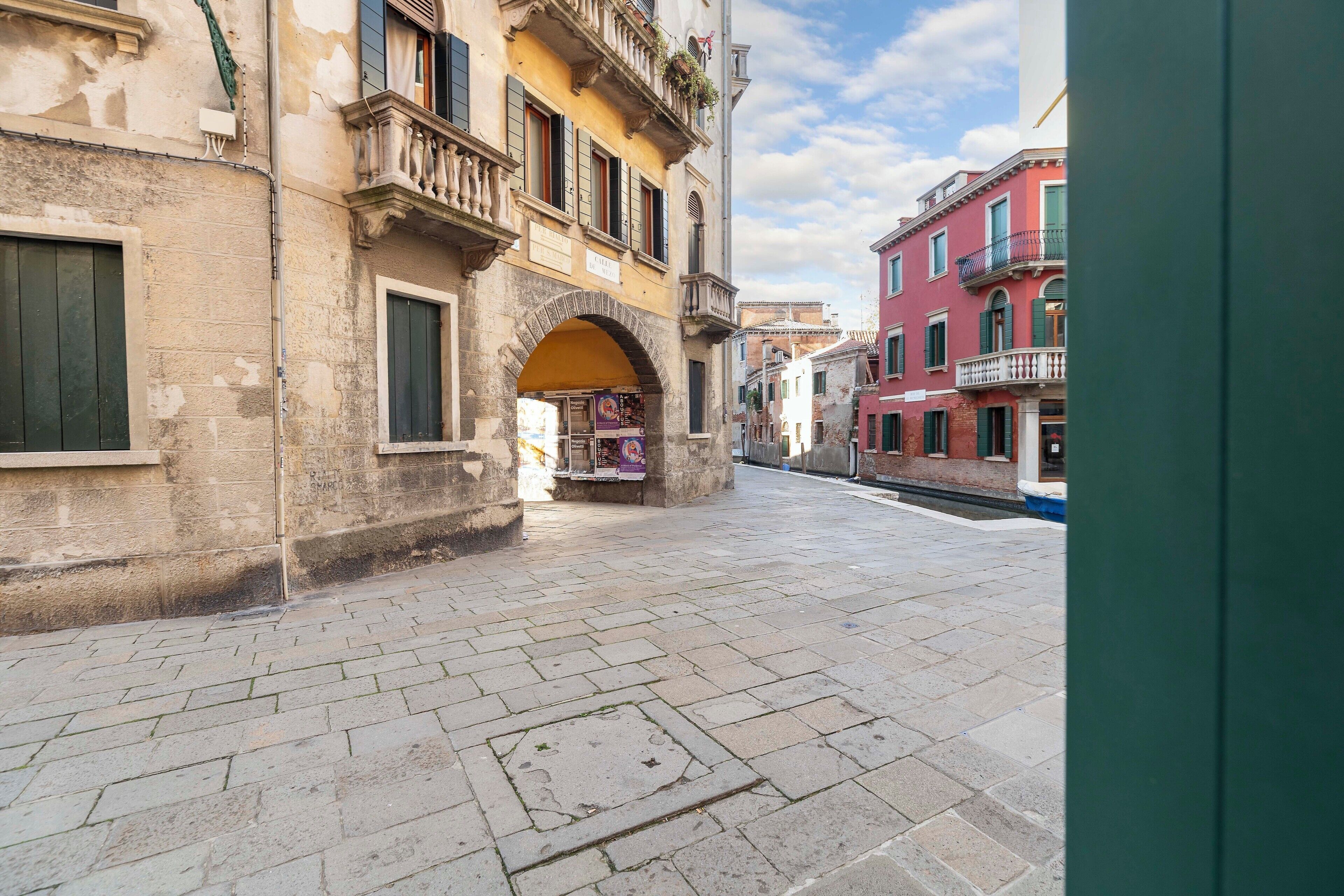 Uma rua estreita com edifícios históricos, um arco e uma pequena loja.