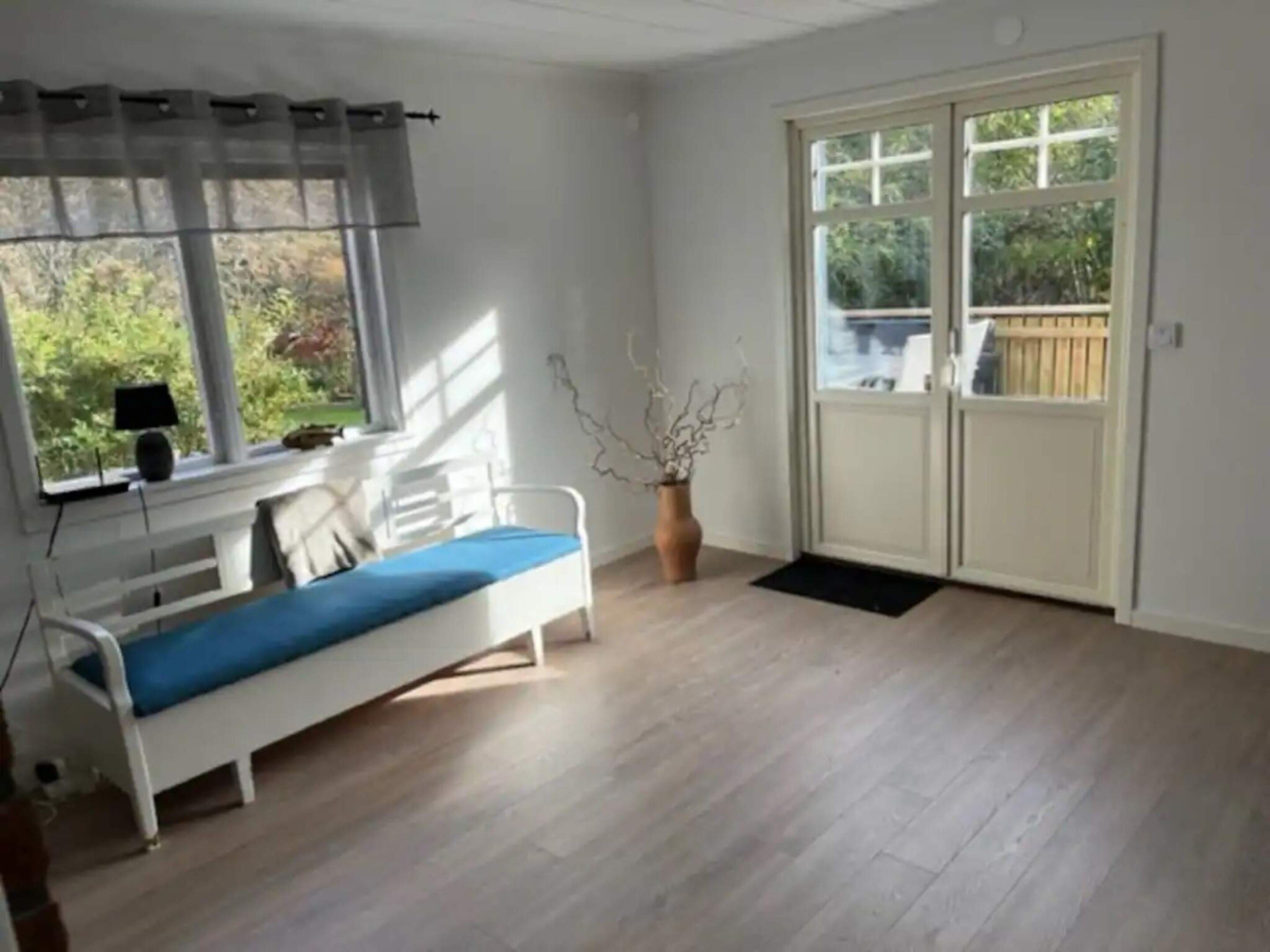 Quarto com cama, janela com cortinas, um vaso de planta e porta de vidro deslizante que dá para o exterior.