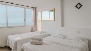 Quarto de hotel com duas camas, uma janela grande com cortinas, um espelho e um interruptor de luz na parede.