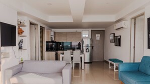 Sala de estar com um sofá cinza, um sofá azul, área de cozinha com geladeira e mesa de jantar.
