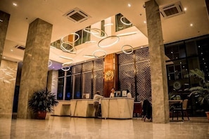 Uma área de recepção de hotel com design moderno, com balcão de atendimento, espaço para sentar e elementos decorativos.