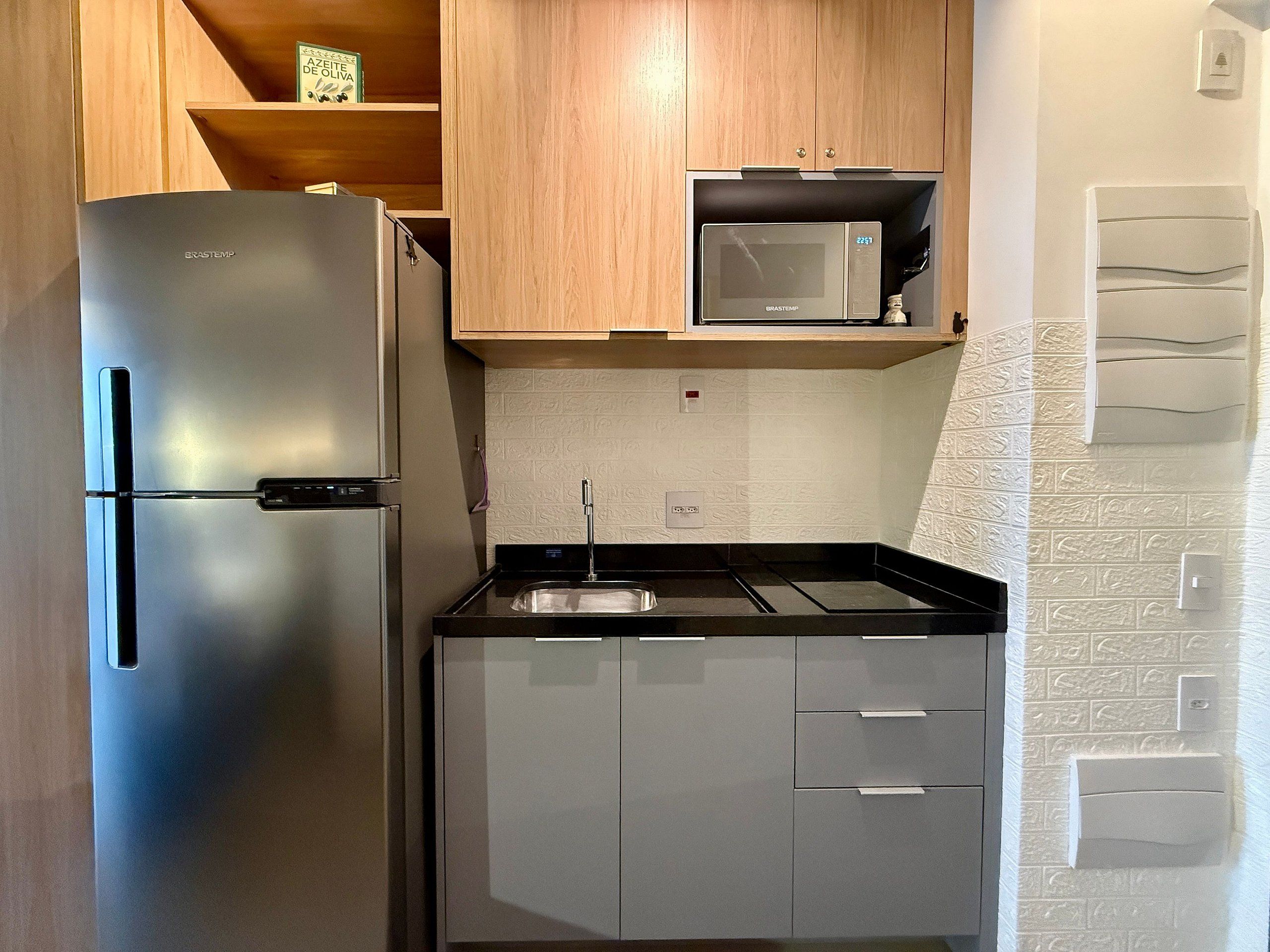 Cozinha compacta com geladeira de aço inoxidável, micro-ondas e pia.