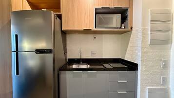 Cozinha compacta com geladeira de aço inoxidável, micro-ondas e pia.