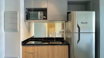 Uma cozinha compacta com micro-ondas, geladeira de aço inoxidável, armários de madeira e bancada preta.