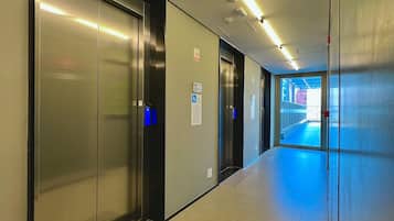 Um corredor com elevadores, um sinal de saída azul e um alarme de incêndio.