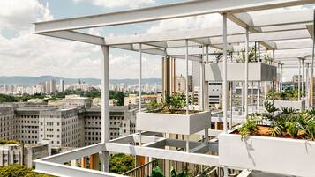 Terraço no telhado com vista para a paisagem urbana, apresentando um design arquitetônico moderno, com elementos estruturais brancos e plantas verdes.
