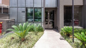 Edifício moderno com fachada de vidro, número 286, e área de entrada bem cuidada com plantas.