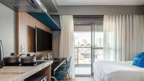 Quarto de hotel moderno com cozinha compacta, cama e vista para a cidade.