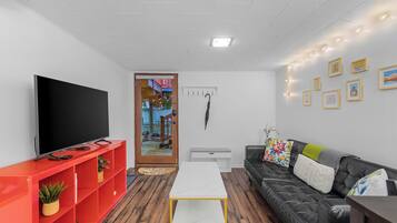 Uma sala de estar moderna com TV de tela plana, estante vermelha, mesa de centro branca, sofá de couro preto e porta que dá para uma área externa.