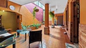 Um p átio interno espaçoso com mesa de vidro, cadeiras de vime e plantas em vasos.