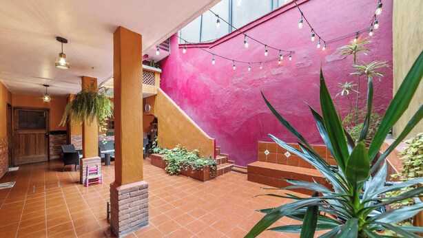 Um espaço amplo e interno com piso de ladrilho terracota, parede rosa e luzes de cordão.