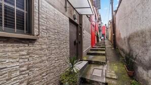Um beco estreito, com uma parede de pedra de um lado e um edifício com toldo metálico do outro.