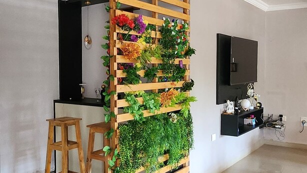 Um quarto com divisória de madeira, jardins verticais, móvel de entretenimento preto e televisão na parede.