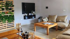Uma sala de estar moderna com uma mesa de jantar de madeira, sofás e uma TV fixada na parede.