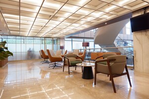 Um hall amplo com assentos modernos, piso lustroso e grandes janelas com vista para o exterior.