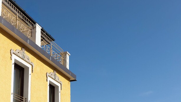 Um edifício amarelo com molduras de janela elaboradas e uma varanda com grades de metal.