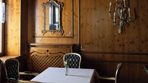 Uma sala de jantar com painéis de madeira, um candelabro, espelho ornamentado e uma mesa com cadeiras.