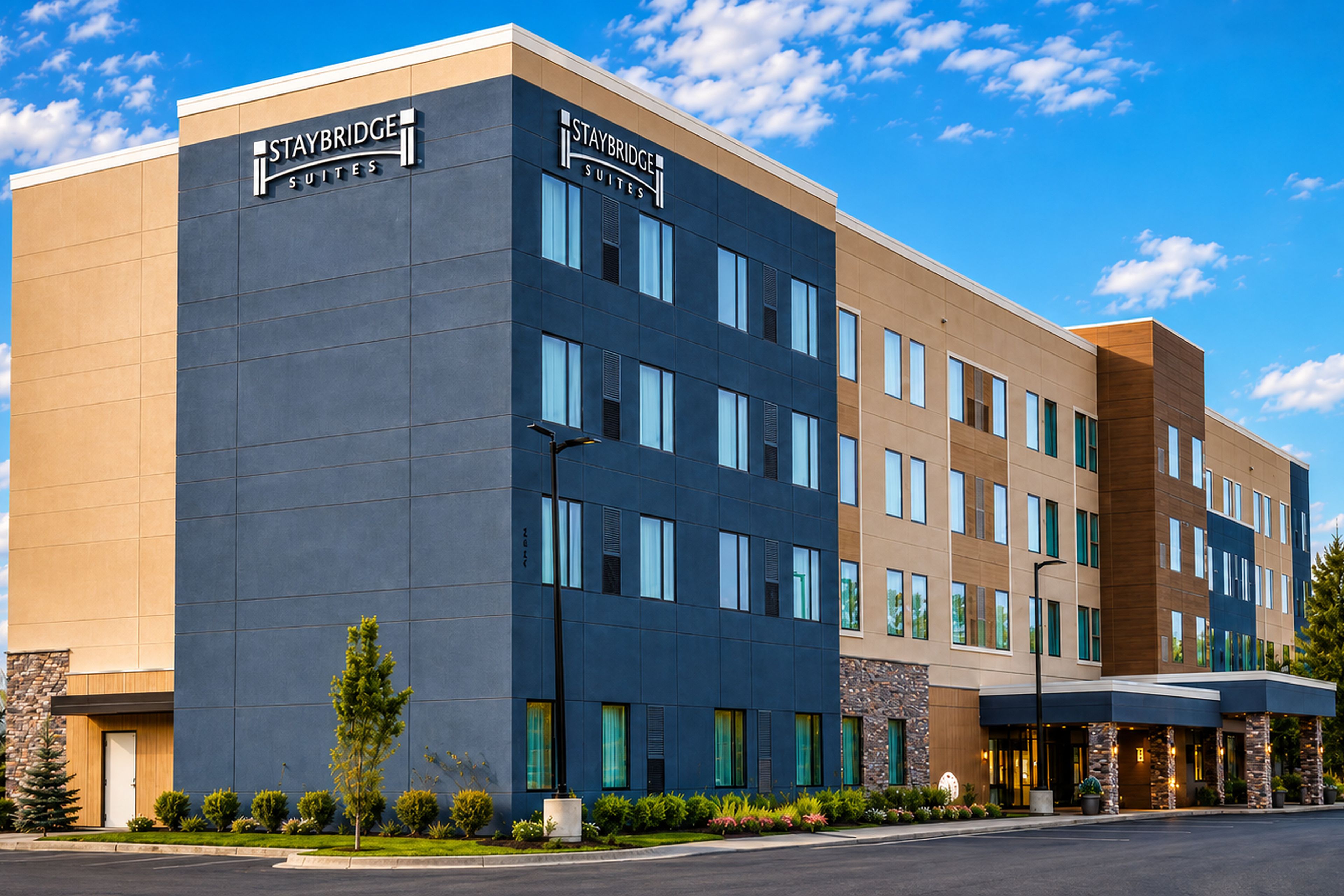Edifício do hotel Staybridge Suites, com design arquitetônico moderno, apresentando uma combinação de fachadas de vidro e pedra, várias janelas e exterior bem cuidado.