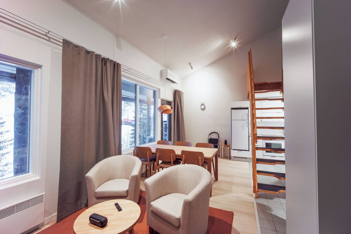 Quarto de hotel moderno com área de refeições, escada de madeira e vista para o exterior.