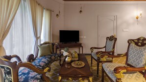 Quarto com sofá, duas cadeiras, mesa de centro, televisão e um vaso decorativo.