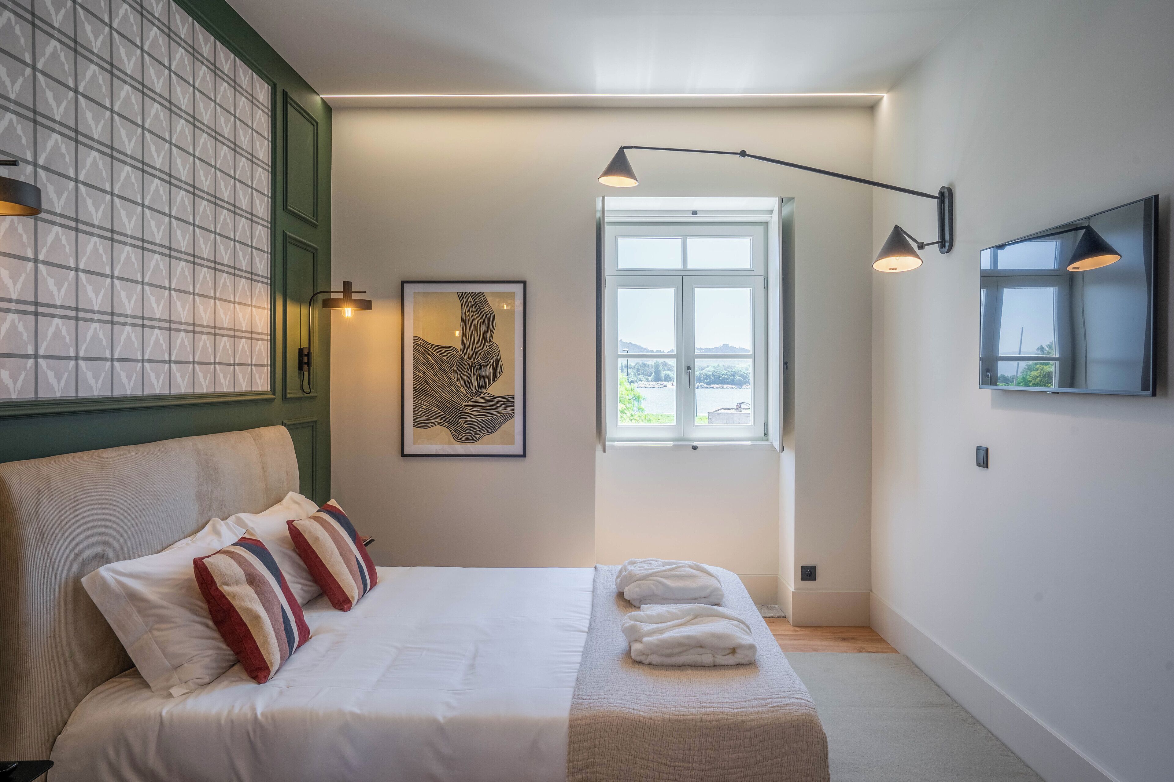 Quarto bem arrumado com cama, almofadas, janela e um quadro.