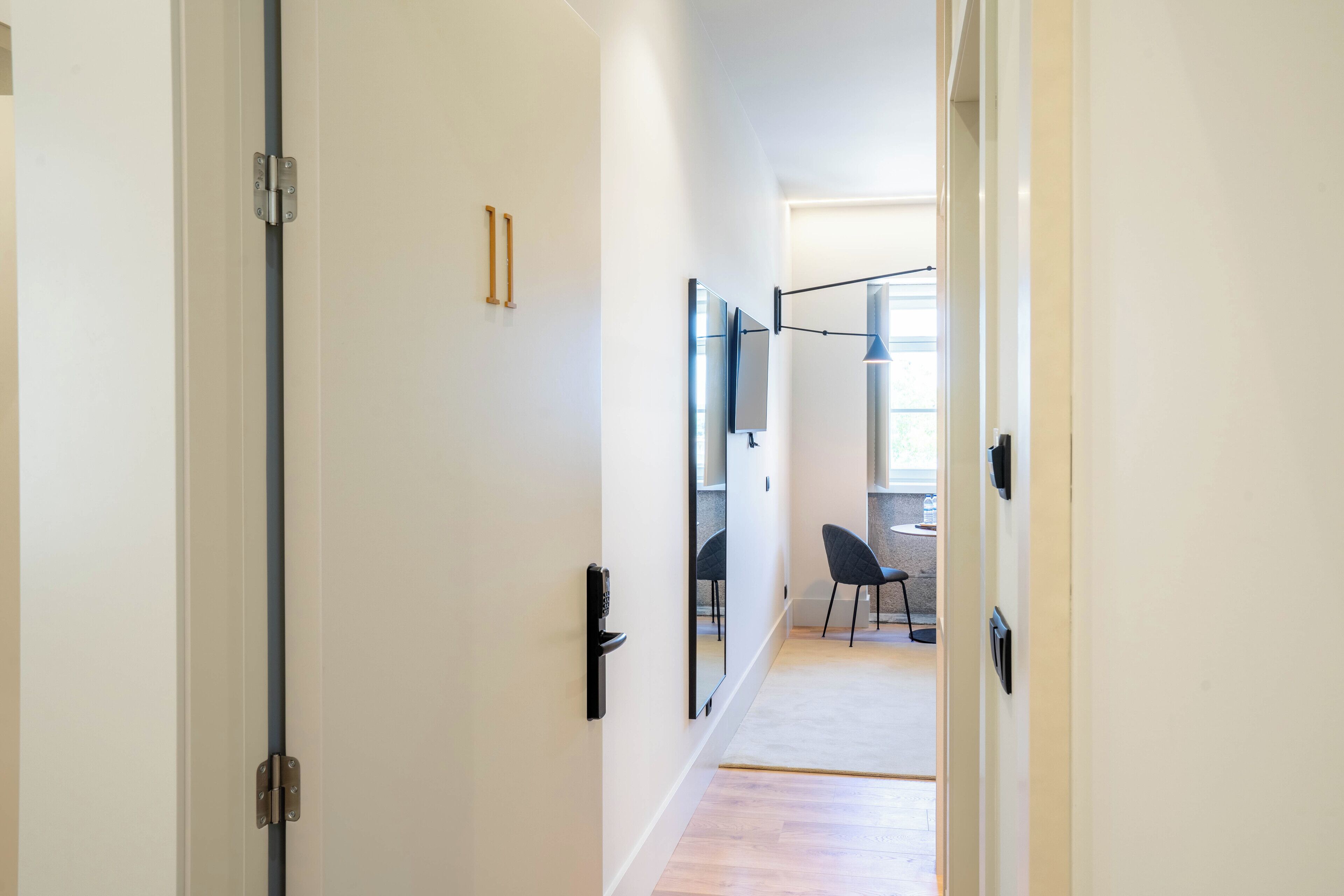Um corredor com uma porta, um luminário fixado na parede e uma cadeira ao fundo.