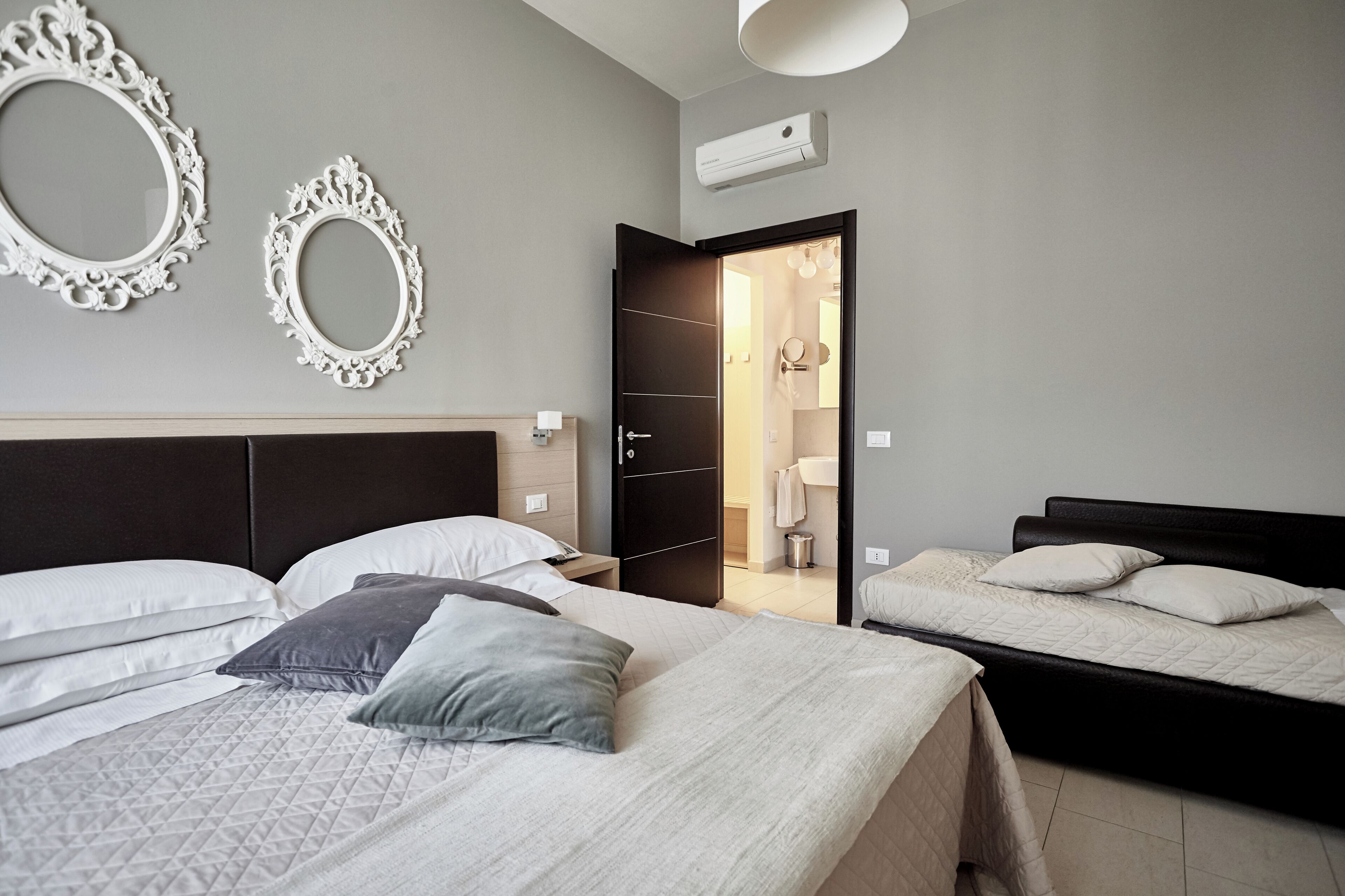 Quarto de hotel com duas camas, um espelho grande e porta de acesso a um banheiro.